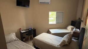 Quarto com duas camas, uma escrivaninha, televisão, ar condicionado e uma janela.
