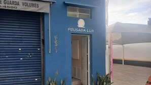 Um edifício azul com o nome 'Pousada Lua' e uma porta azul com persiana fechada.