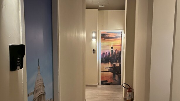 Corredor com um mural do Capitólio, um extintor de incêndio e uma porta com interruptor de luz.