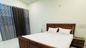 Cama bem arrumada com cabeceira de madeira em quarto limpo e bem iluminado, com paredes brancas e piso ladrilhado.