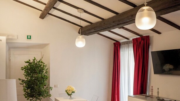 Uma sala de estar moderna com teto de madeira, um sofá, uma mesa de jantar com cadeiras, um vaso com planta e uma TV em um móvel.