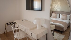 Quarto de hotel moderno com uma cama, uma mesa de trabalho com cadeira, televisão e um espelho grande.