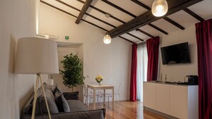 Uma sala de estar moderna com sofá, mesa de jantar com cadeiras, televisão e área de cozinha com bancada e cortinas vermelhas.