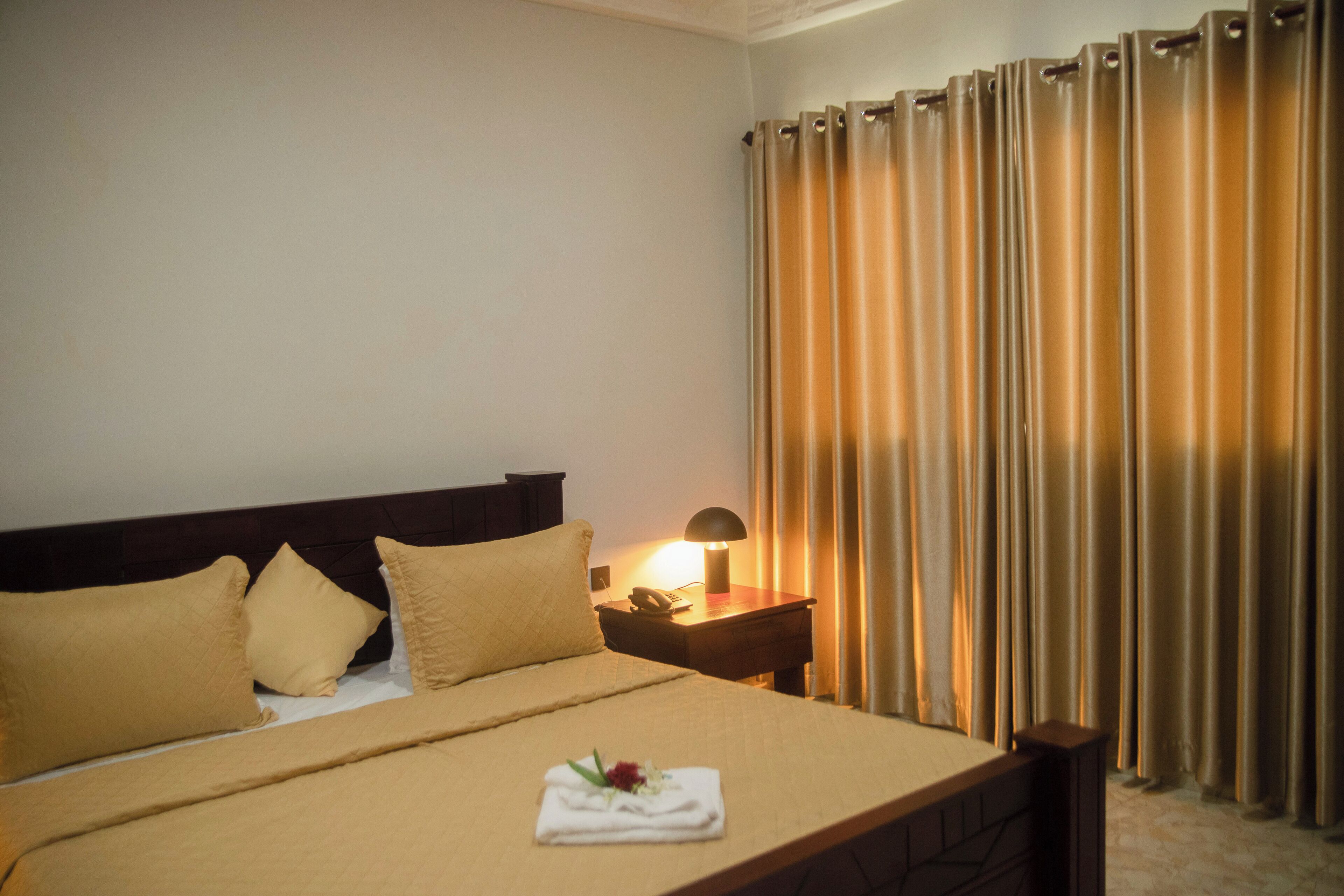 Quarto de hotel com uma cama, mesa de cabeceira, abajur e cortinas.