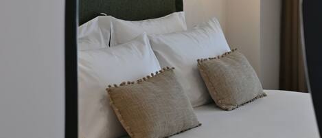 Cama bem arrumada com almofadas brancas e bege, cabeceira verde e luminária pendente.