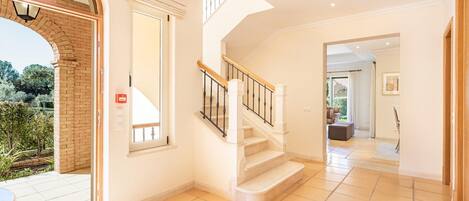 Um interior espaçoso com uma escadaria em curva, um arco de tijolos e vista para o exterior.