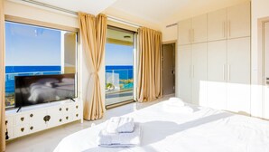 Quarto de hotel com uma cama grande, televisão, varanda com cortinas e vista para o mar.