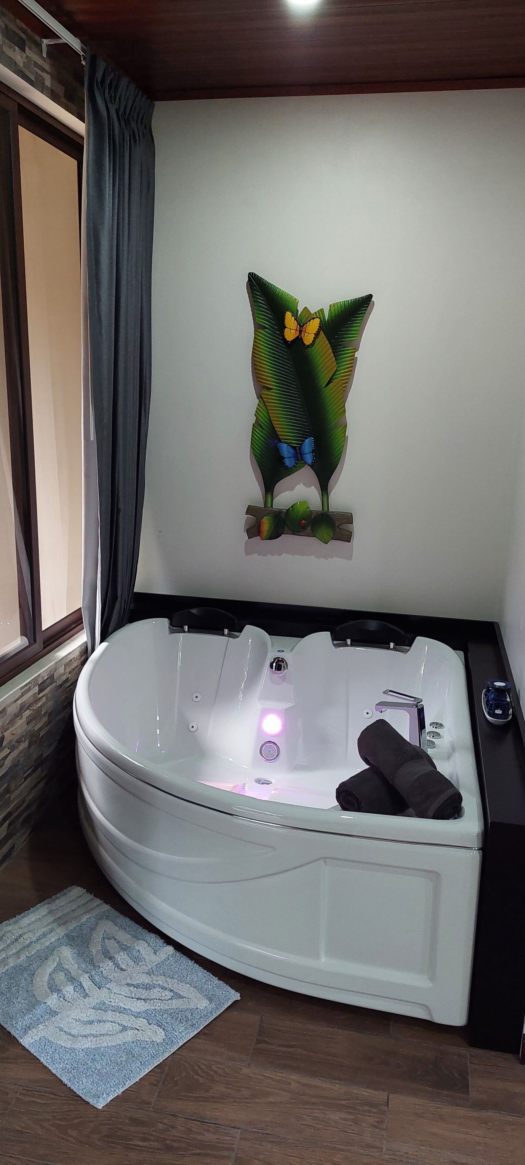 Um quarto de spa com uma banheira de hidromassagem branca, uma peça decorativa na parede e um tapete azul estampado.