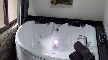 Um quarto de spa com uma banheira de hidromassagem branca, uma peça decorativa na parede e um tapete azul estampado.