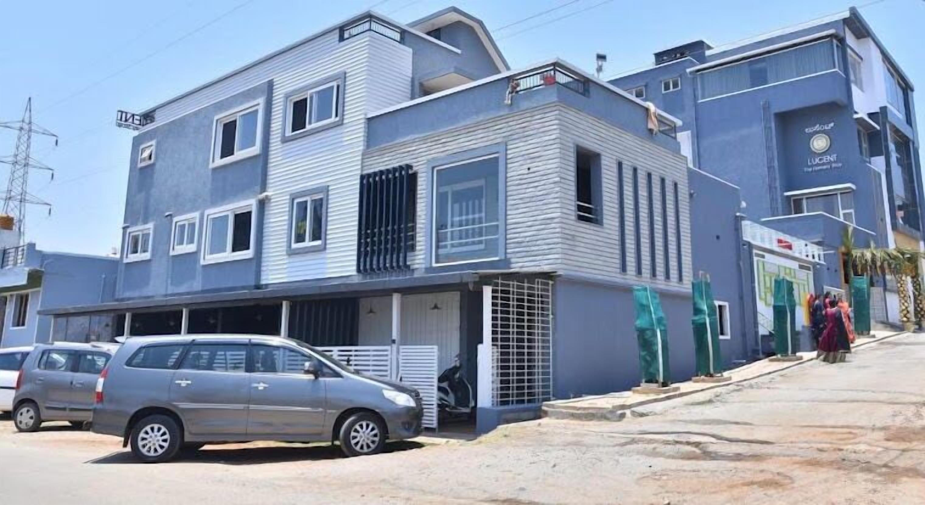 Um edifício de dois andares com uma garagem, um carro estacionado em frente e uma pessoa perto da entrada.