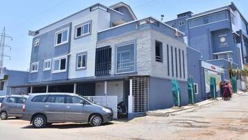 Um edifício de dois andares com uma garagem, um carro estacionado em frente e uma pessoa perto da entrada.