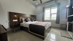Quarto de hotel moderno com uma cama grande, televisão de tela plana, ventilador de teto e janela com cortinas.