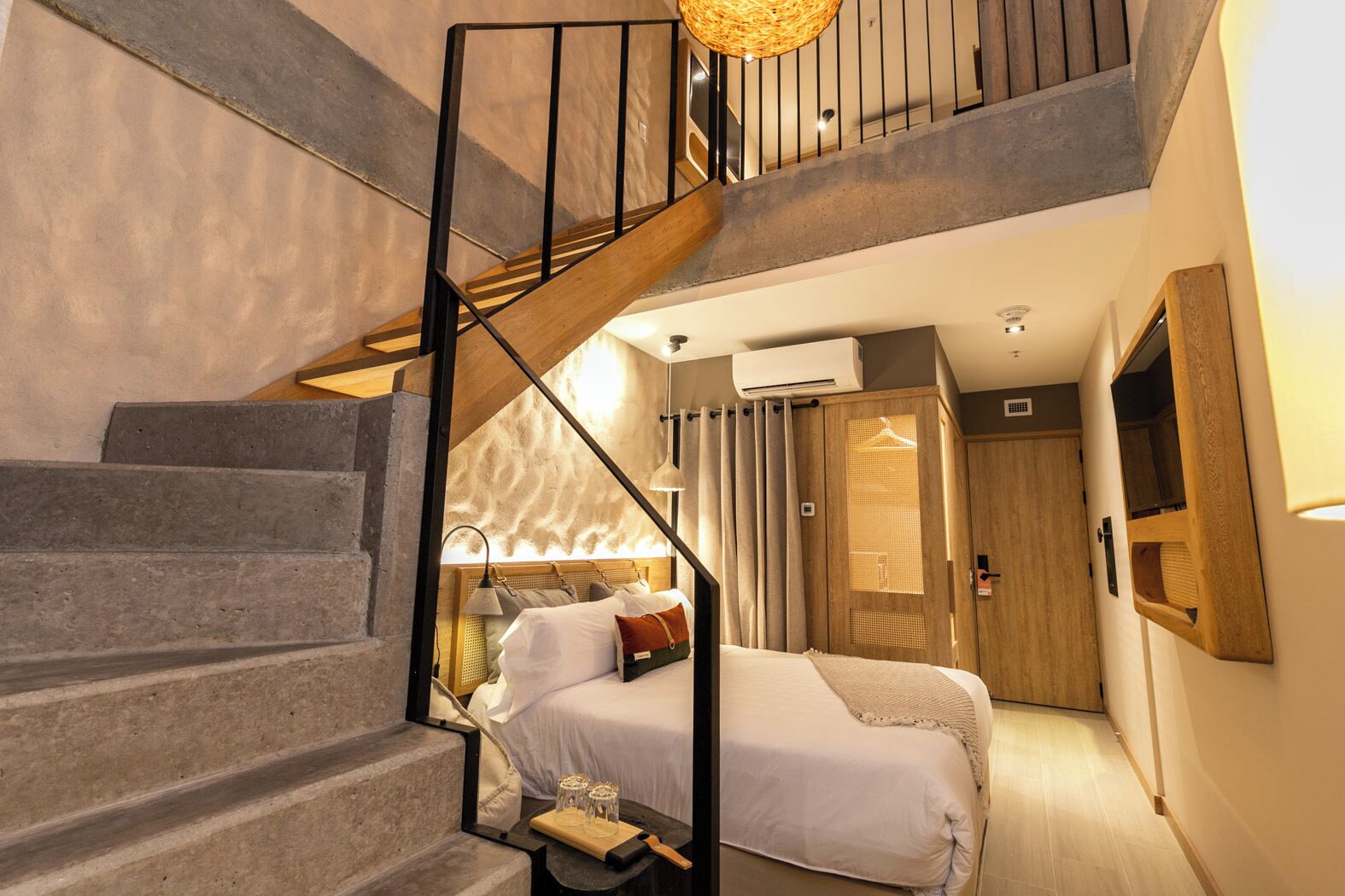 Uma escadaria que leva a um quarto com cama, mesa de cabeceira e luminária pendente.