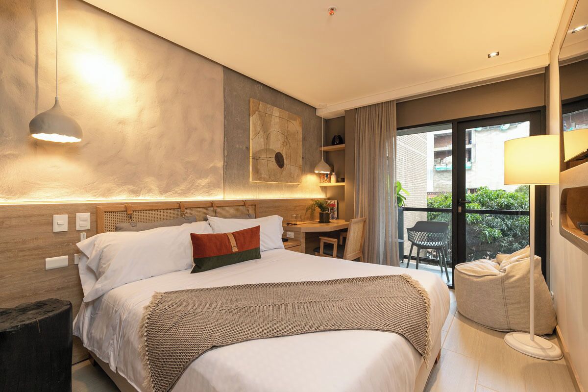 Quarto de hotel com uma cama grande, uma escrivaninha, uma cadeira e varanda com vista.