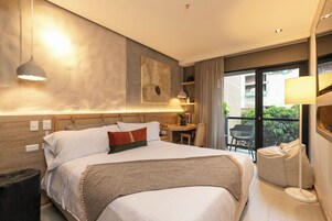 Quarto de hotel com uma cama grande, uma escrivaninha, uma cadeira e varanda com vista.