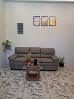 Uma sala de estar com um sofá, uma mesa de centro com uma bandeja de petiscos, duas plantas em vasos e três quadros na parede.