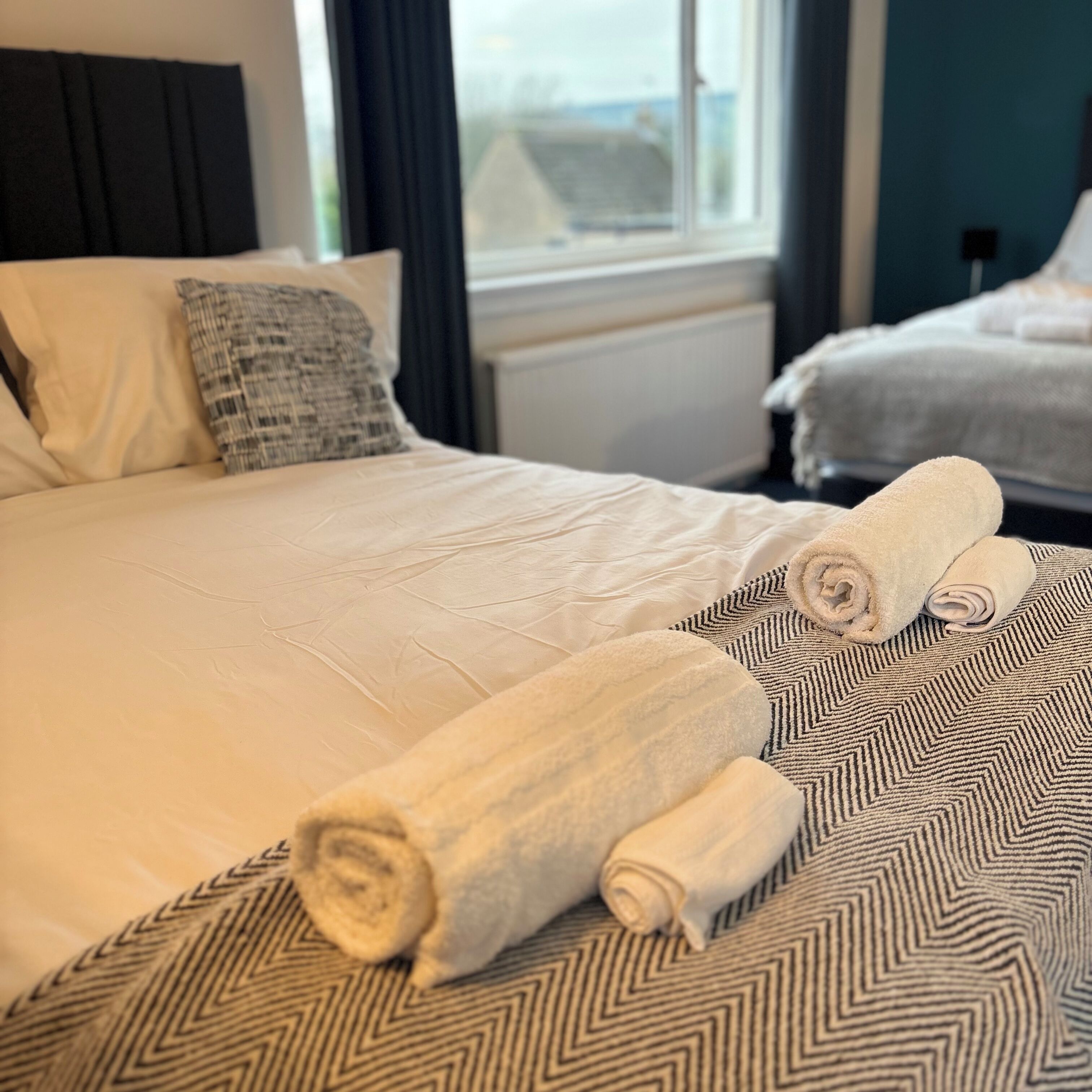 Quarto de hotel com uma cama bem arrumada, um tapete estampado e vista para o exterior através de uma janela.