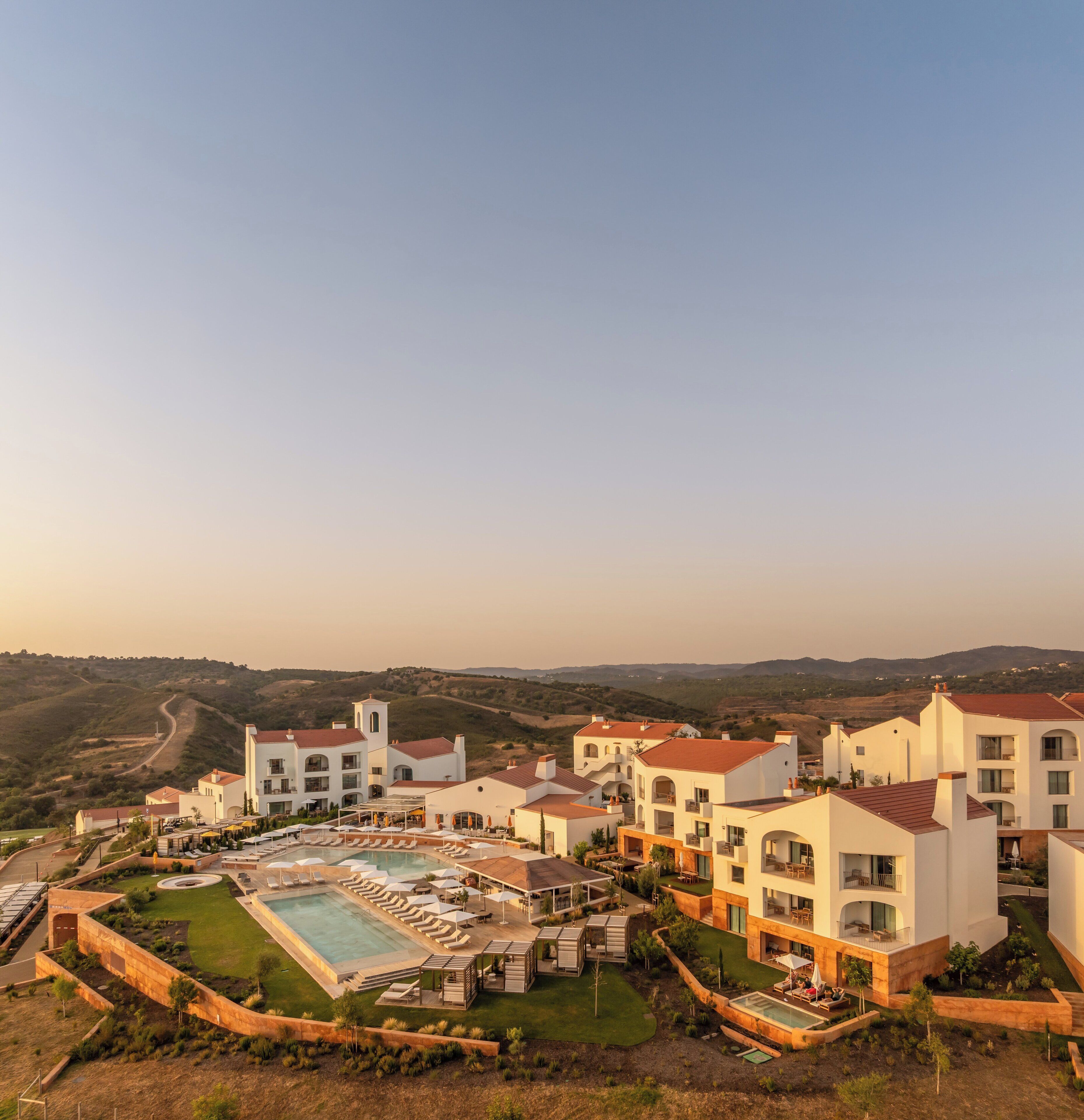 Um resort com vários edifícios, piscina e paisagem montanhosa ao fundo.