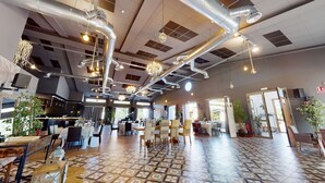 Um restaurante amplo com pé direito alto, dutos aparentes e piso de azulejos estampados.