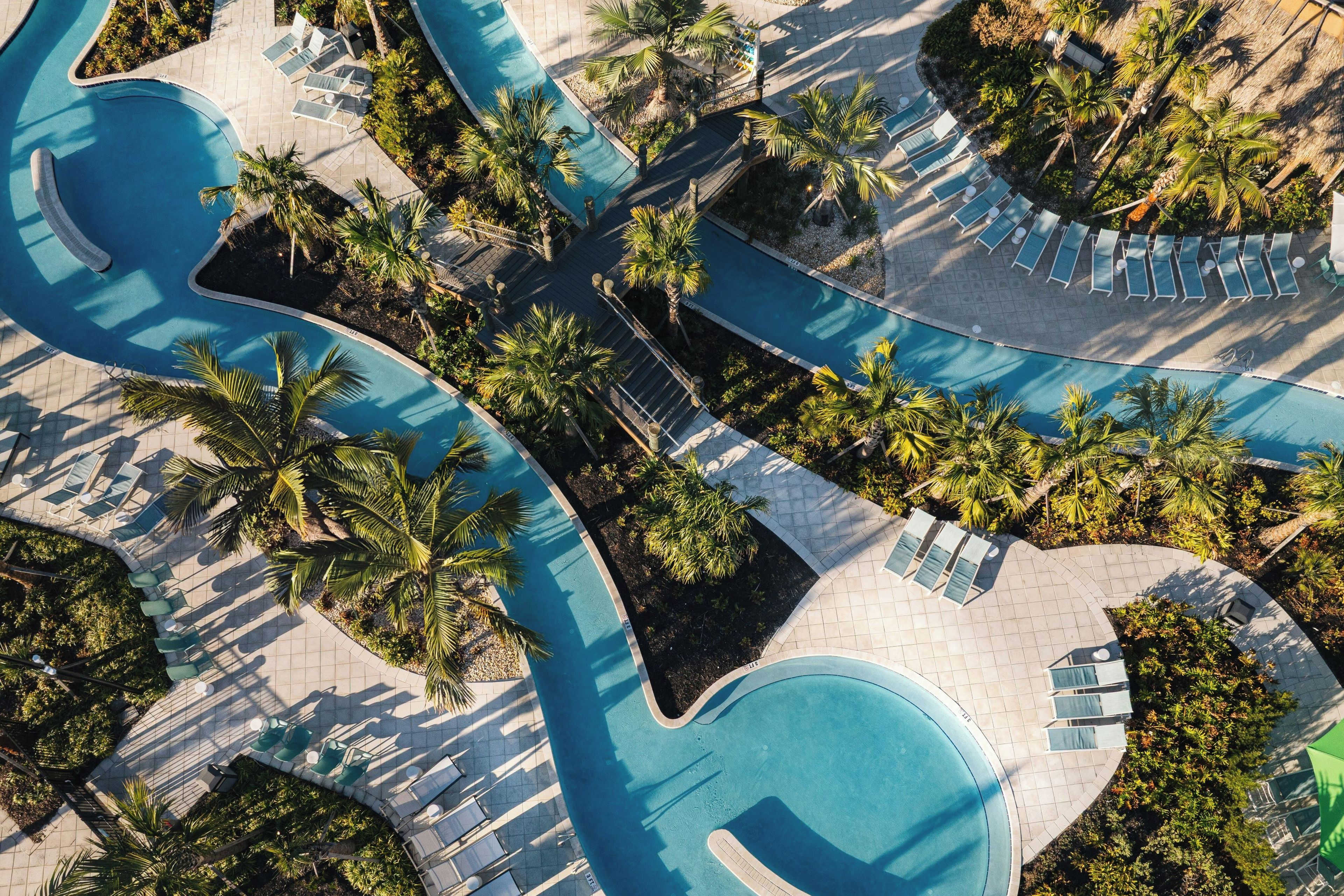 Área de piscina com várias piscinas, espreguiçadeiras e palmeiras.