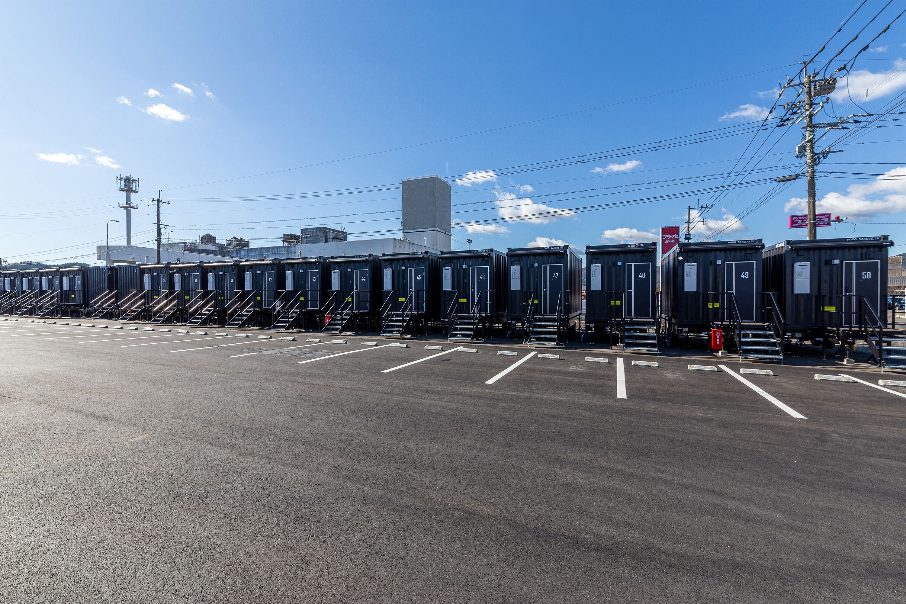 Uma fileira de banheiros químicos com cabines numeradas num parque de estacionamento.