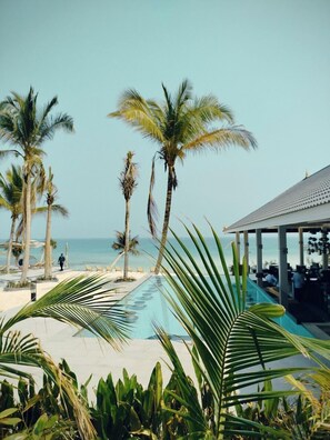 Uma área à beira da piscina com palmeiras, um espaço de estar coberto e vista para o oceano.