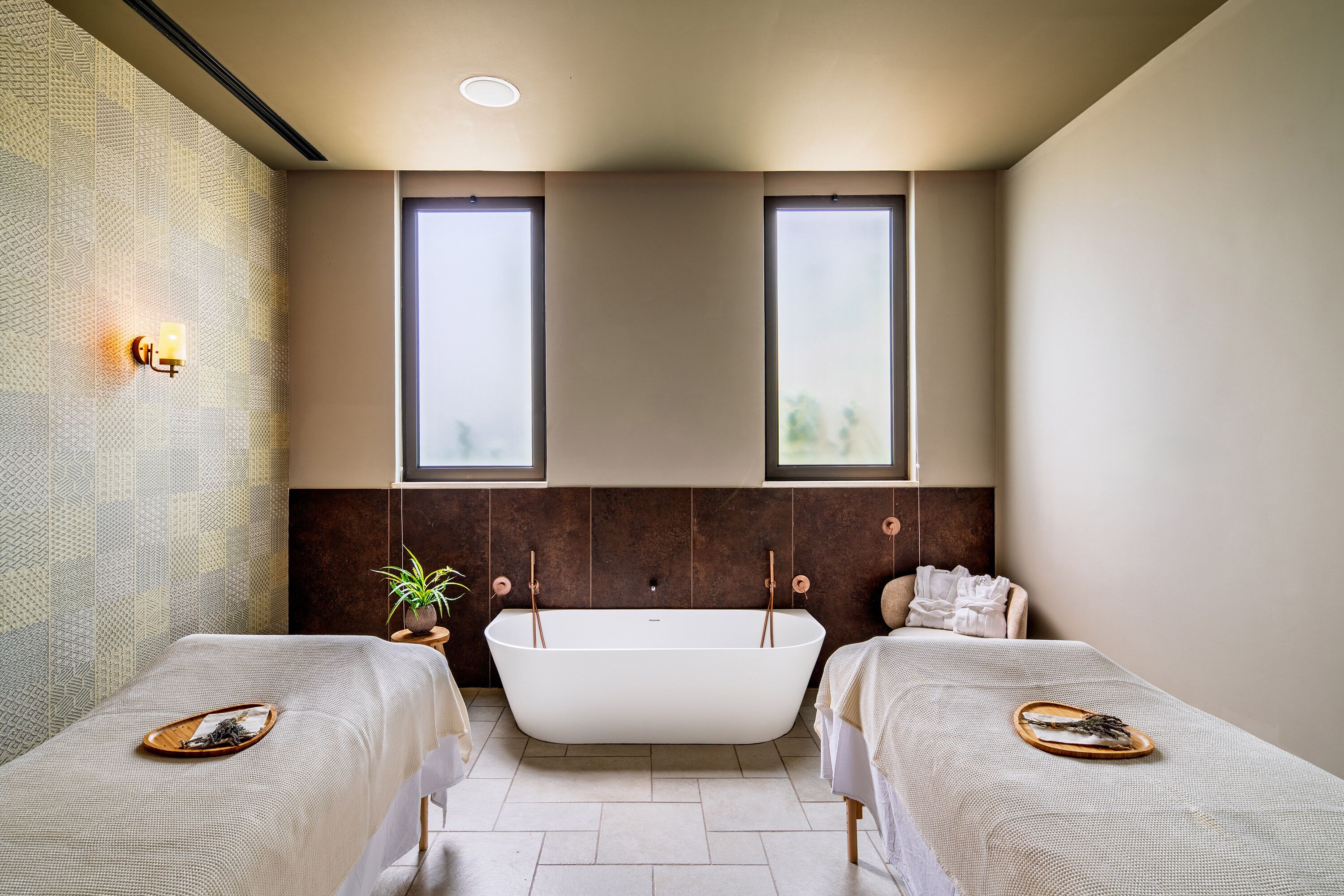 Um quarto de spa com uma banheira de imersão, duas camas e um luminário fixado na parede.