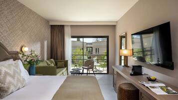 Quarto de hotel com cama, escrivaninha com televisão de tela plana, mesa pequena com cadeira, janela com vista para o exterior e varanda com mesa e cadeiras.