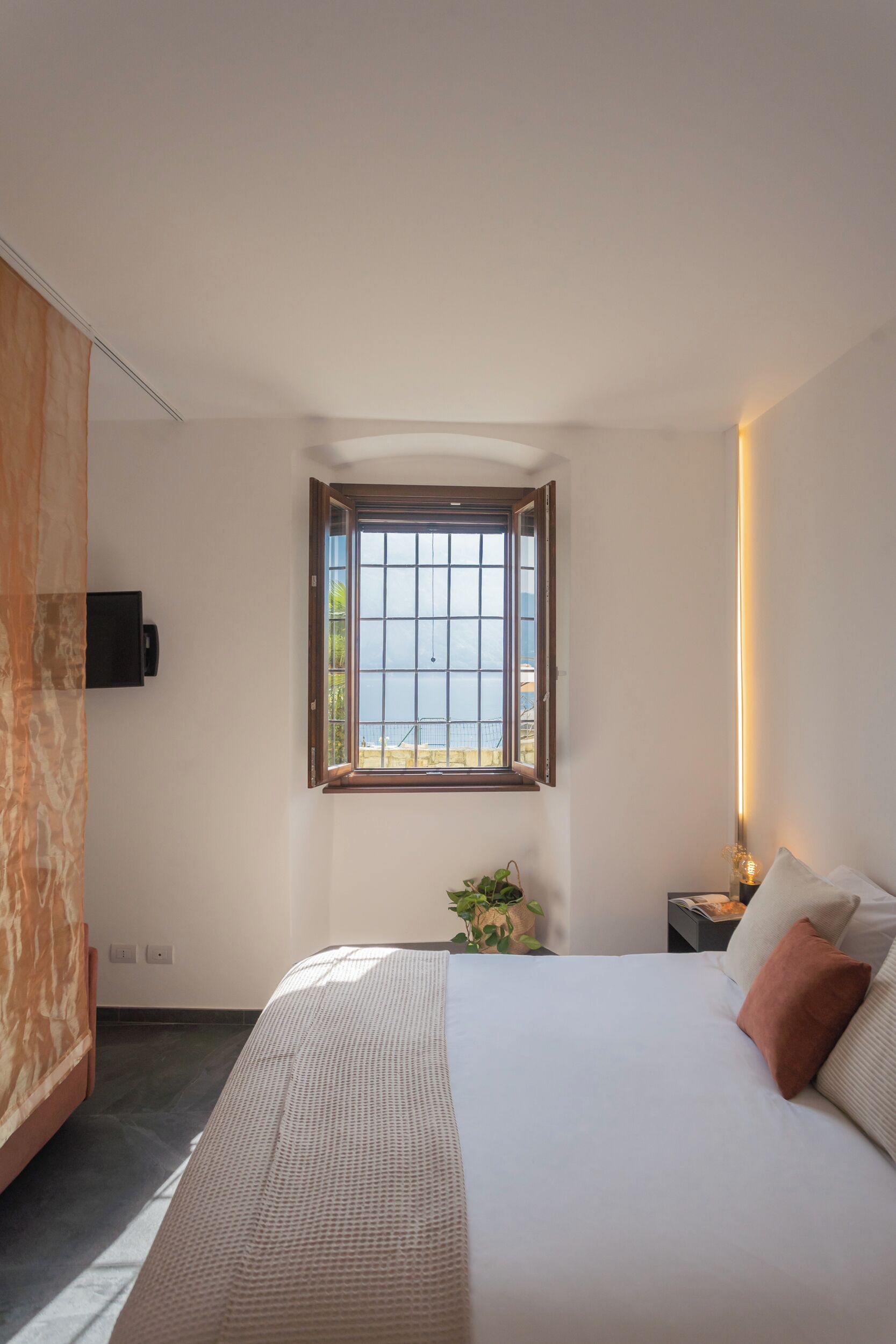 Quarto com cama grande, janela vista para o mar, televisão fixada na parede e mesa de cabeceira com luminária.