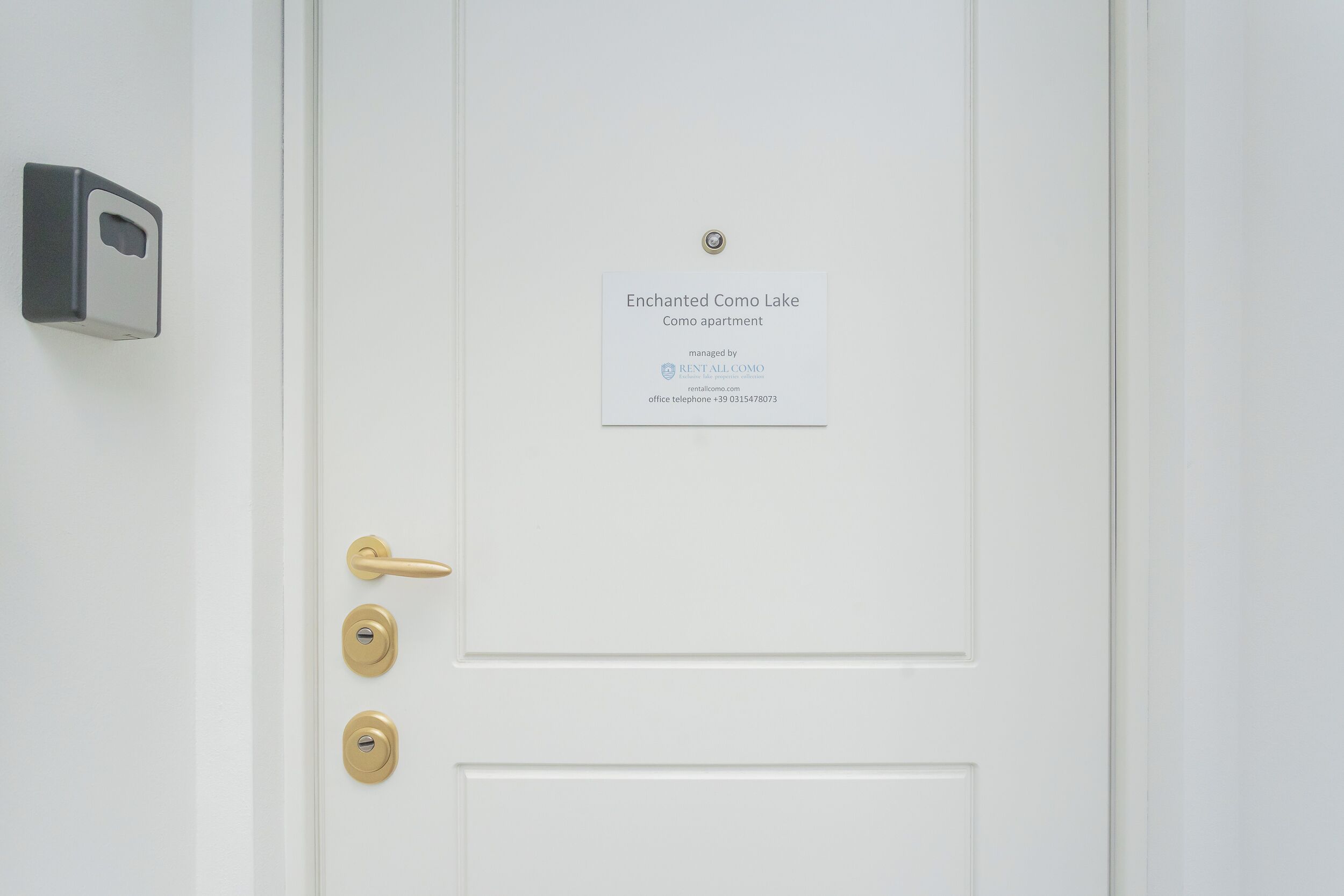 Uma porta branca com uma fechadura, um interfone e uma placa indicando apartamento da RENT ALL COMO.