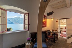 Um quarto acolhedor com vista para um lago, uma área de refeições com mesa e cadeiras, e uma pequena mesa lateral com um vaso de flores.