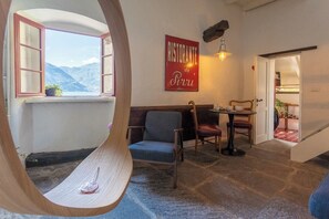 Uma área de refeições acolhedora com um banco de madeira, uma mesa com cadeiras e vista para montanhas pela janela.