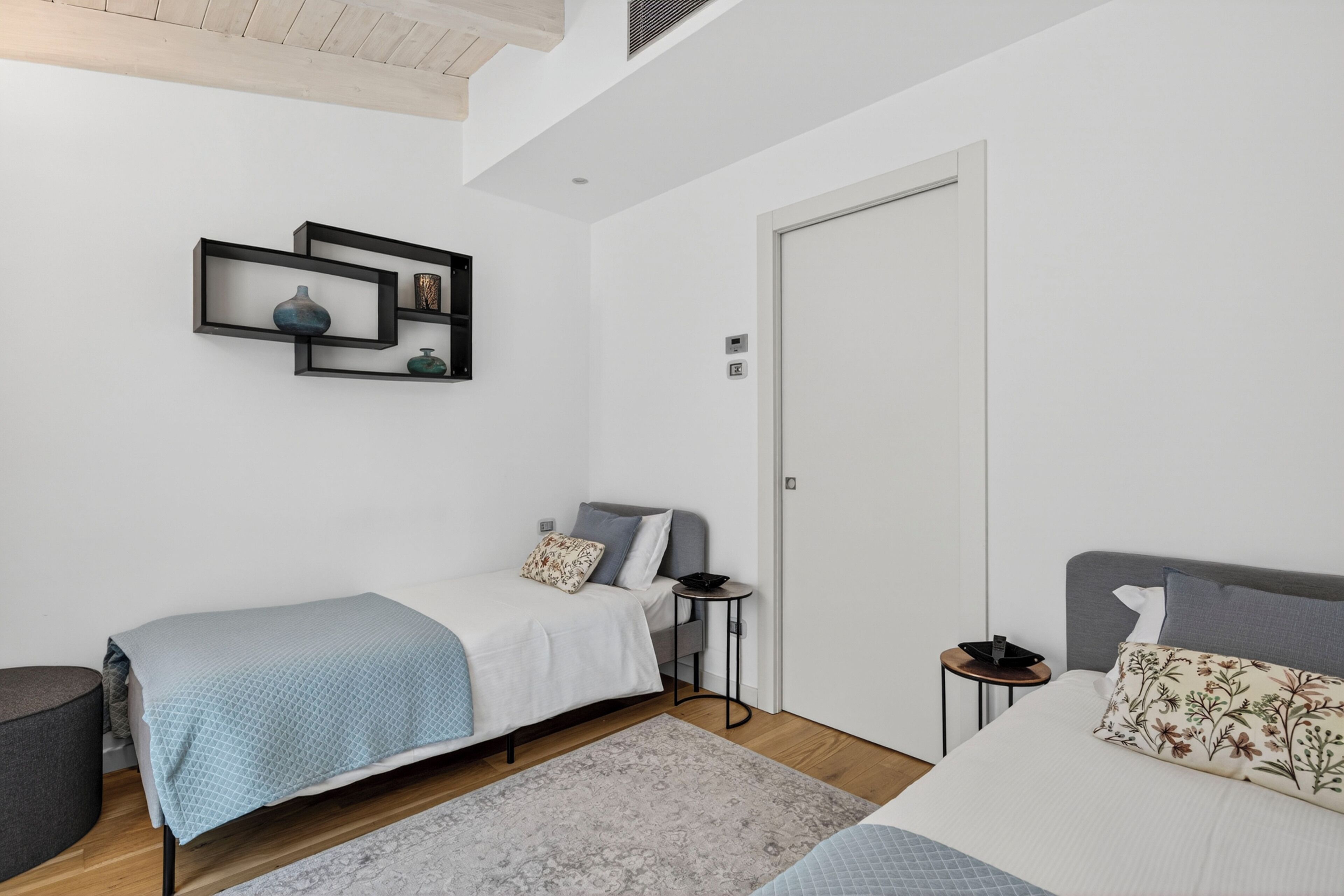 Quarto moderno com cama, mesas de cabeceira, guarda-roupa e prateleira na parede com objetos decorativos.