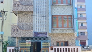 Um edifício com vários andares, fachada estampada, entrada com portão e placa com 'Mayur Shines'.