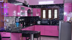 Cozinha com armários rosa, bancada preta e uma geladeira.
