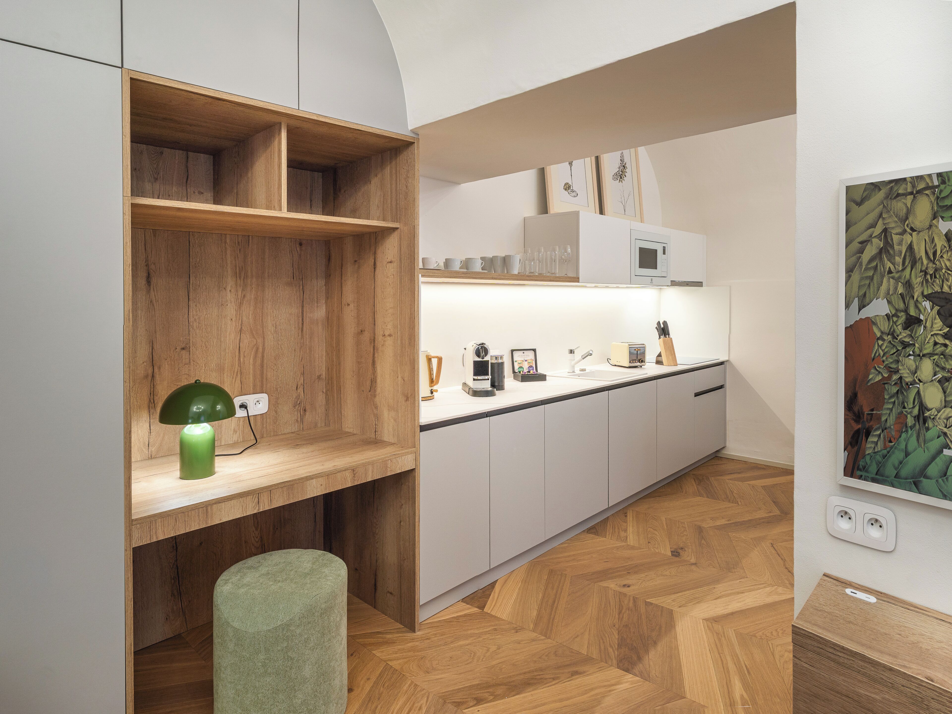 Uma cozinha moderna com prateleiras de madeira, uma luminária verde e piso de madeira em padrão herringbone.
