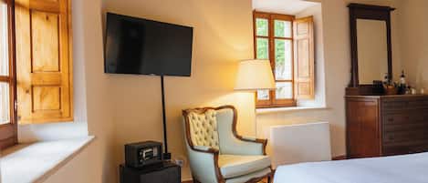 Quarto com cama, televisão na parede, cómoda de madeira e uma cadeira.