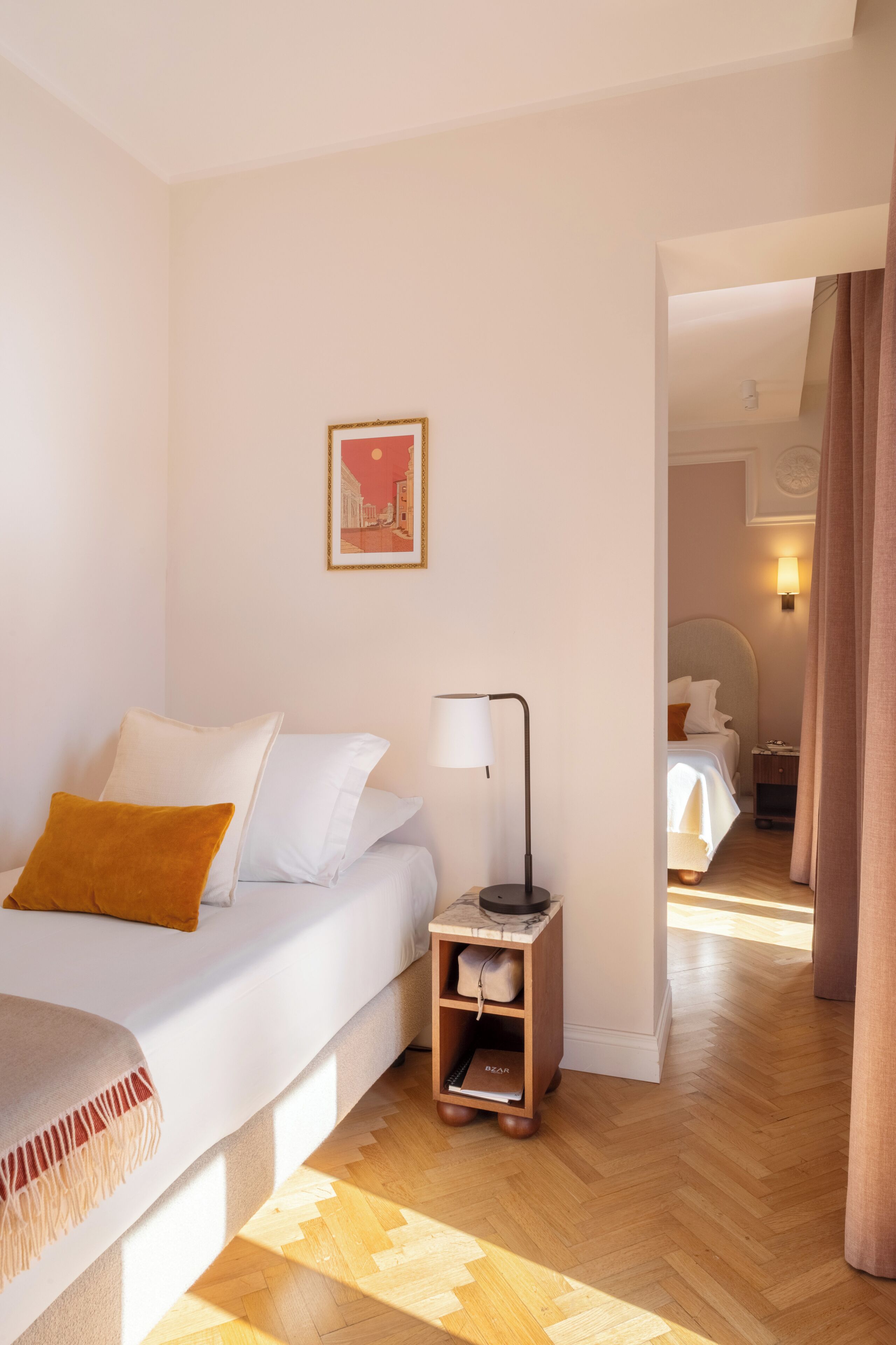 Quarto de hotel com cama, mesa de cabeceira, luminária e um quadro na parede.