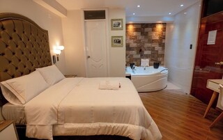Quarto de hotel com uma cama grande, banheiro com banheira e uma pequena mesa.