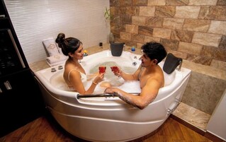 Um casal em uma banheira de hidromassagem, com parede de pedra e piso de madeira.