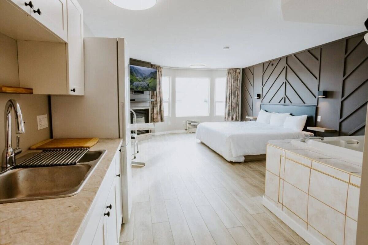 Quarto de hotel moderno com cozinha, uma cama grande e vista para o exterior.
