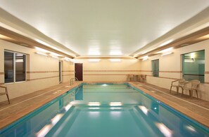 Piscina interna com chão em mosaico, escada e cadeiras nas laterais.