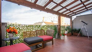 Terraço no telhado com um banco de madeira, uma mesa pequena e plantas em vasos.