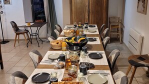 Uma sala de jantar com uma mesa comprida posta para várias pessoas, rodeada de cadeiras.