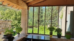Um quarto com paredes de pedra, teto de madeira, uma janela com vista para o verde e algumas plantas em vasos.