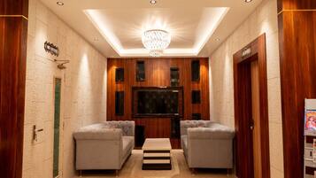 Um hall moderno com um candelabro, uma televisão de tela plana grande e dois sofás.