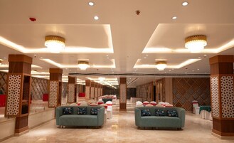 Um amplo hall de hotel com teto alto, lustres modernos e uma área de estar central com sofás.