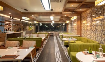 Um restaurante com assentos em verde, mesas redondas, soalho estampado e um bar com prateleiras de garrafas.