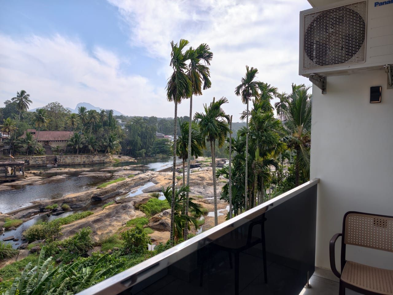 Varanda com vista para um rio e palmeiras, uma cadeira e um aparelho de ar condicionado.