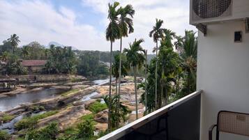 Varanda com vista para um rio e palmeiras, uma cadeira e um aparelho de ar condicionado.